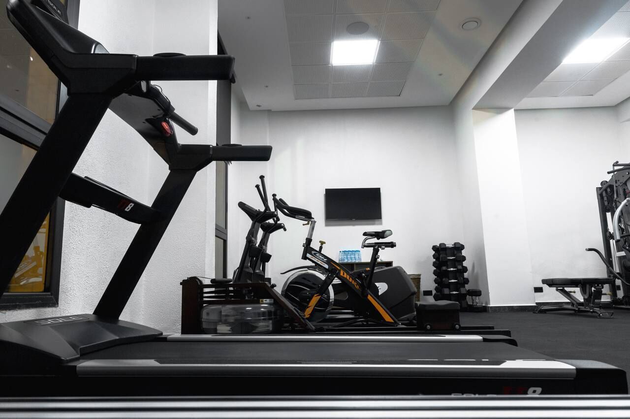 Uma academia com esteira, bicicletas ergométricas e equipamentos de musculação.