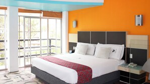 Quarto de hotel moderno com uma cama grande, uma mesinha de vidro e vista pelas portas de vidro.