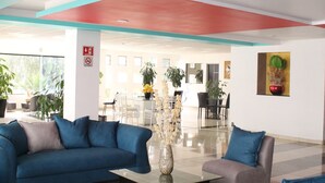 Um hall amplo com sofás azuis, uma mesa de centro e uma área de refeições ao fundo.