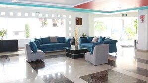 Um hall moderno com um sofá azul, uma mesa de centro de vidro e um vaso com plantas secas.