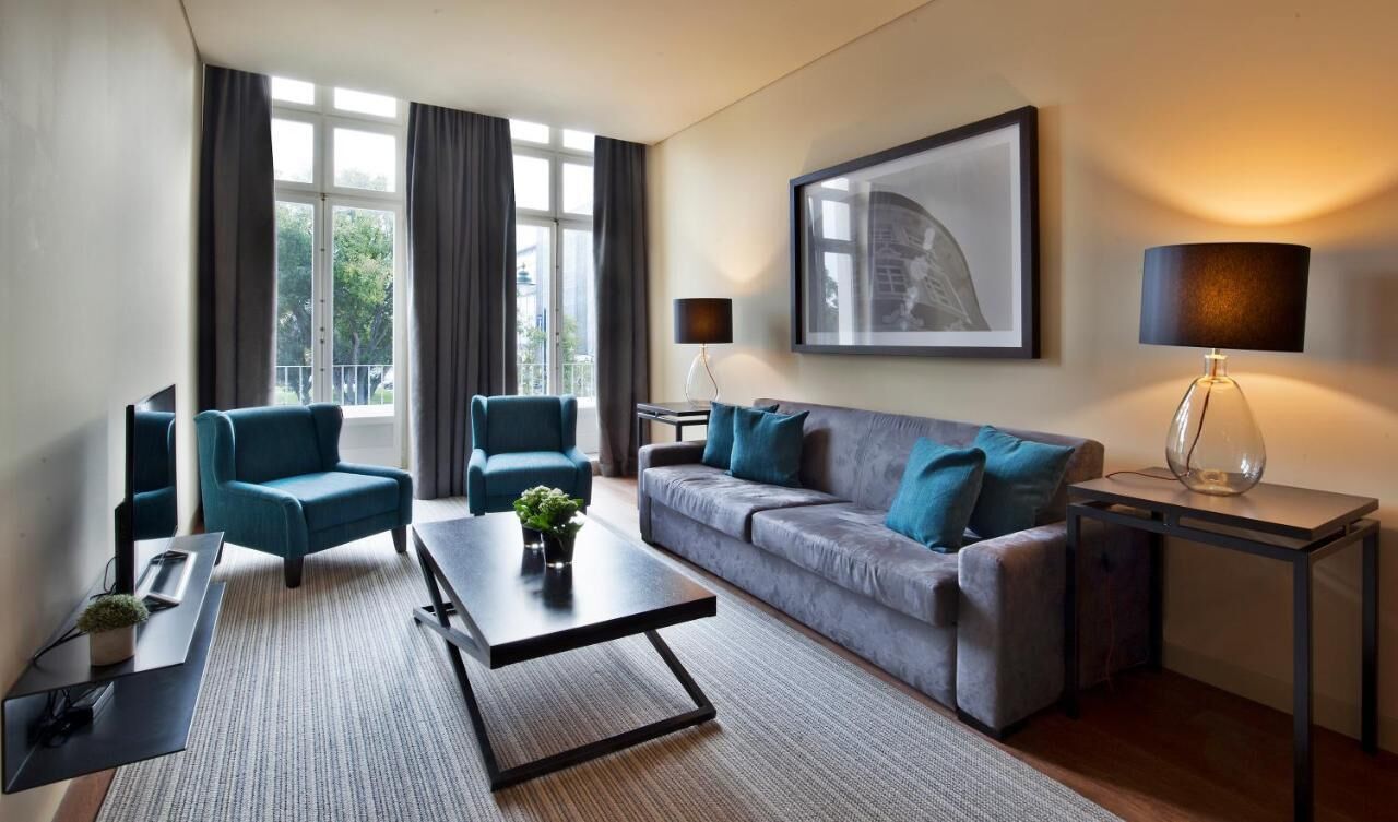 Uma sala de estar moderna com um sofá cinzento, duas poltronas verde-água, uma mesa de centro, uma TV e um quadro na parede.