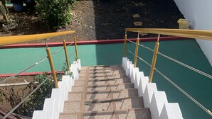 Degraus externos com piso de azulejos estampados, guarda-corpos brancos e uma parede verde ao fundo.