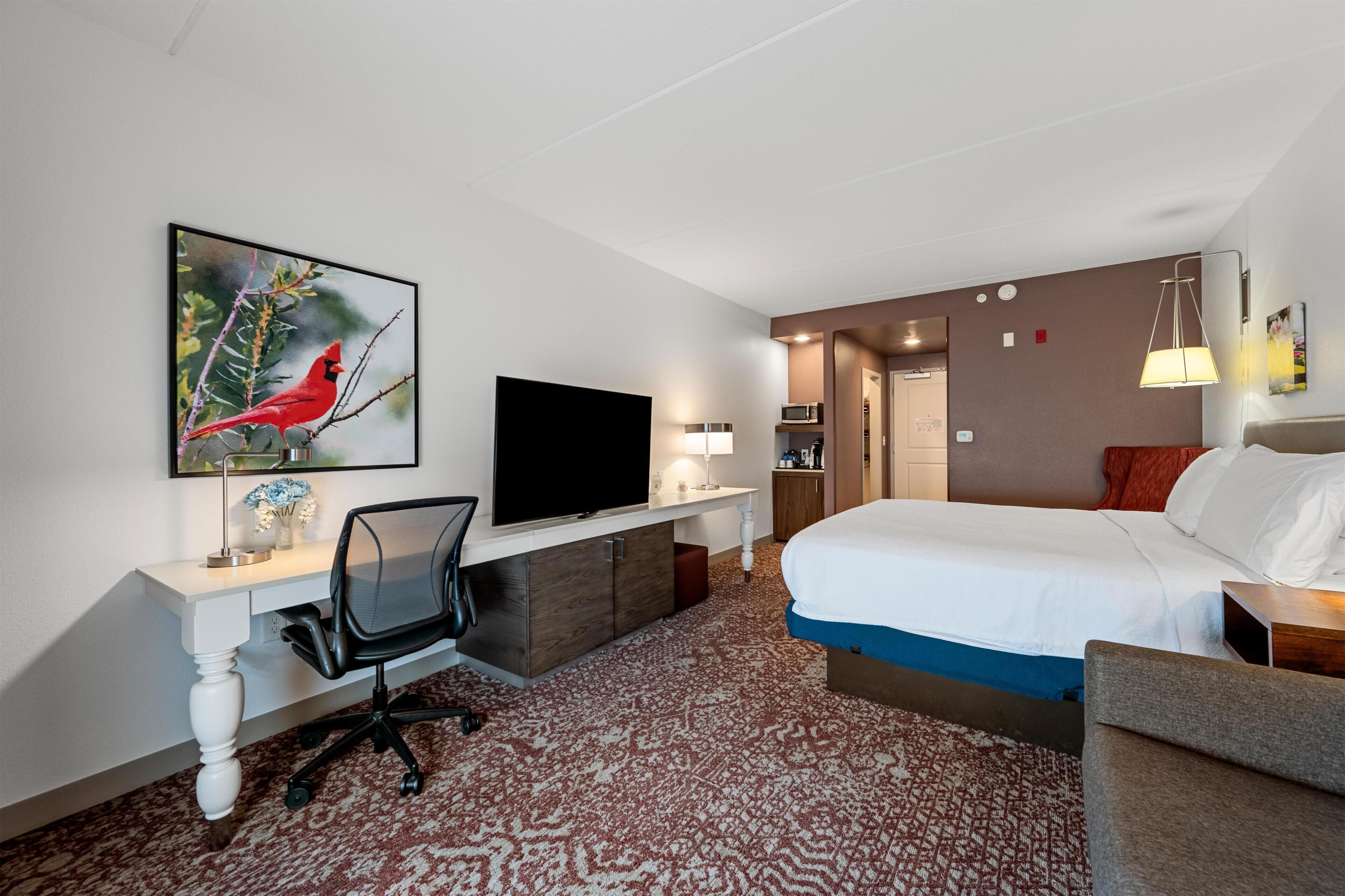Quarto de hotel com cama, escrivaninha, televisão e obras de arte.