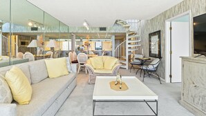 Uma sala de estar ampla com sofá, cadeiras, mesa de centro e escada que leva a um andar superior.