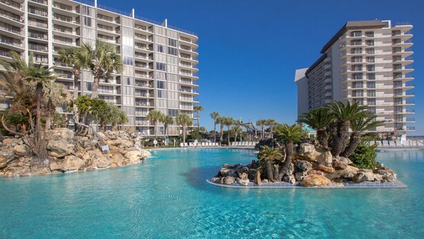 Um resort com uma grande área de piscina, palmeiras e edifícios altos ao fundo.