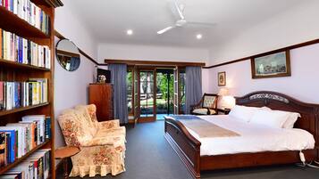 Quarto com uma cama grande, uma cadeira, uma estante de livros e vista através de uma porta de vidro.
