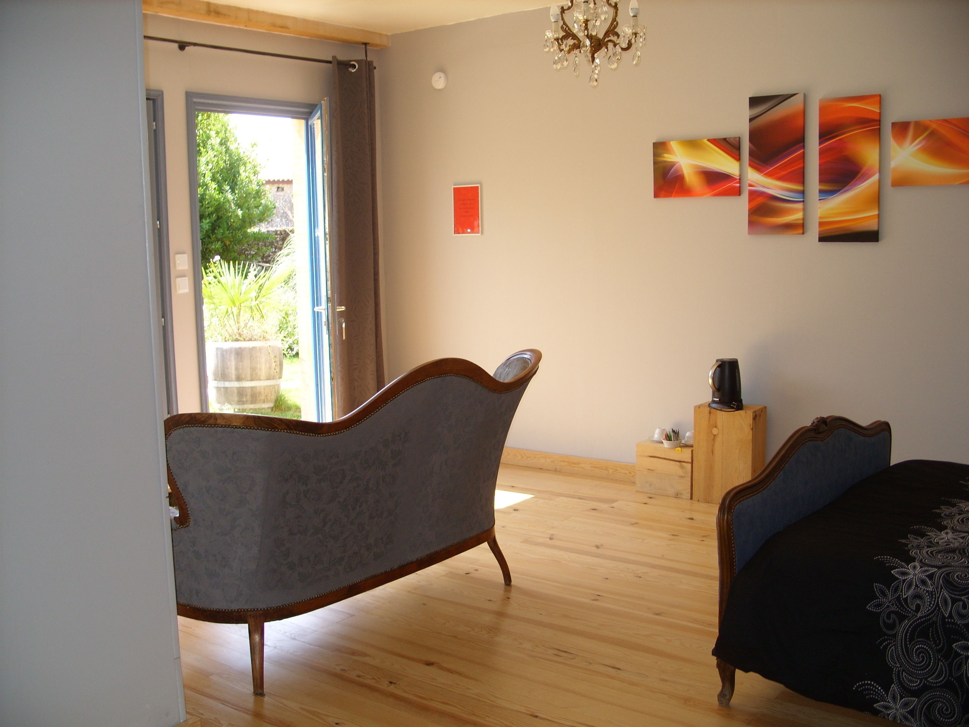 Quarto com piso de madeira, cama, cadeira, lustre e vista através de uma porta.