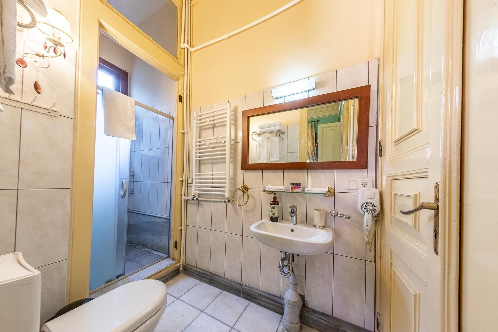 Casa de banho com sanita, lavatório, espelho, porta-toalhas e zona de duche.