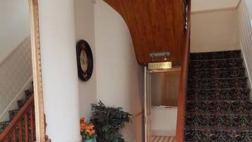 Uma área de recepção com teto de madeira, piso xadrez e escada com grades ornamentadas.