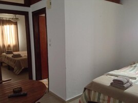 Quarto de hotel com uma cama, uma mesa com controle remoto e um banheiro visível por uma porta aberta.