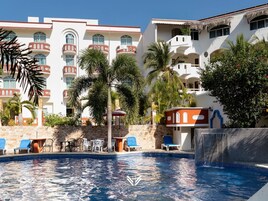 Um hotel com piscina, palmeiras e céu azul.