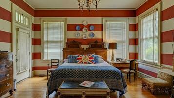 Quarto com uma cama grande, cômoda de madeira, escrivaninha e lustre.