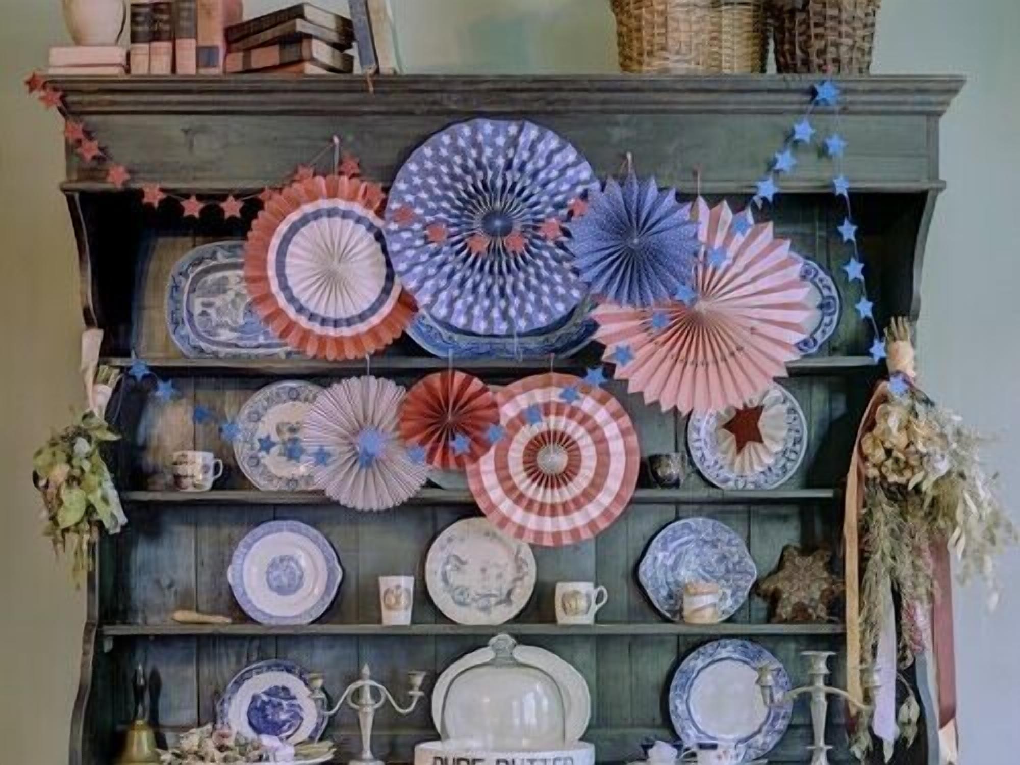 Uma prateleira de madeira com diversos objetos decorativos, incluindo leques de papel, pratos e um abajur de estilo vintage.