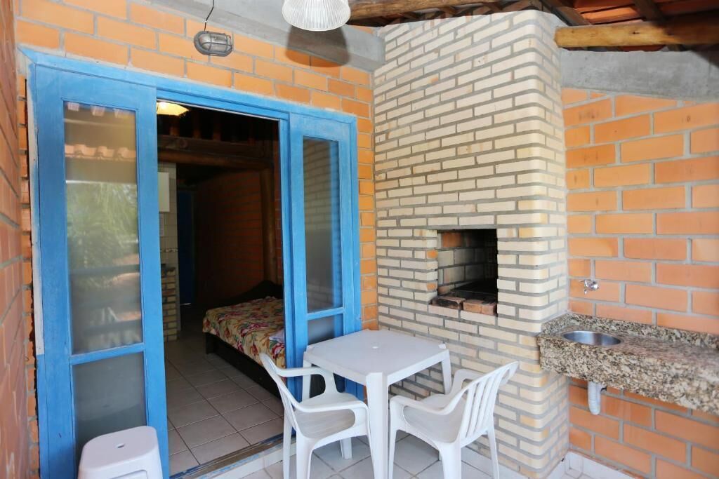 Um quarto pequeno com lareira de tijolos, porta com moldura azul e uma mesa branca com cadeiras.