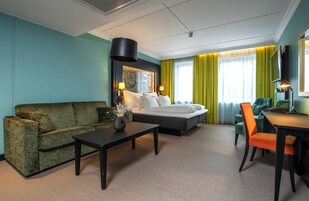 Quarto de hotel com cama, sofá, mesa de jantar e televisão.