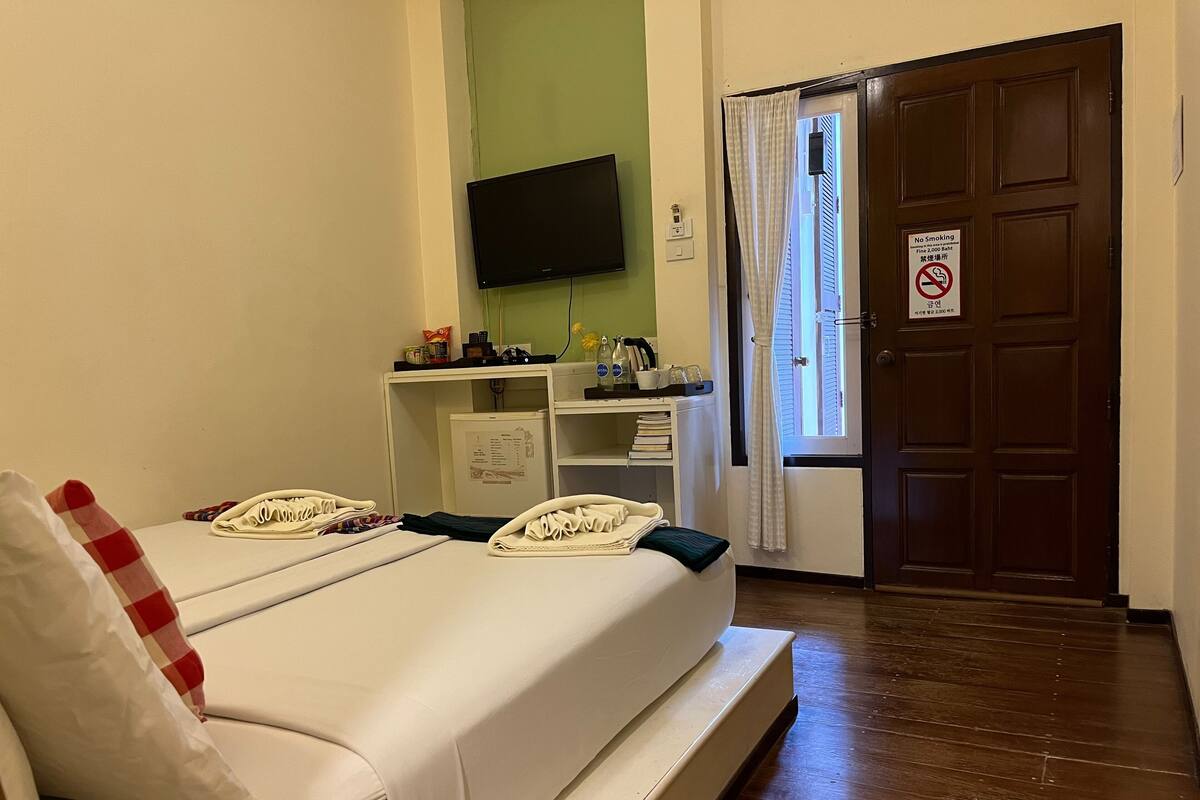 Quarto de hotel com cama, escrivaninha, computador, televisão e porta com placa de proibido fumar.