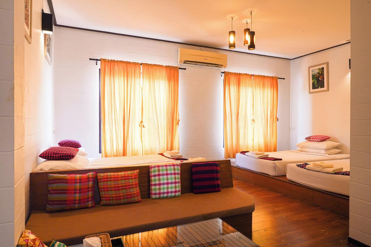 Quarto de hotel com duas camas, um banquinho e uma mesinha.