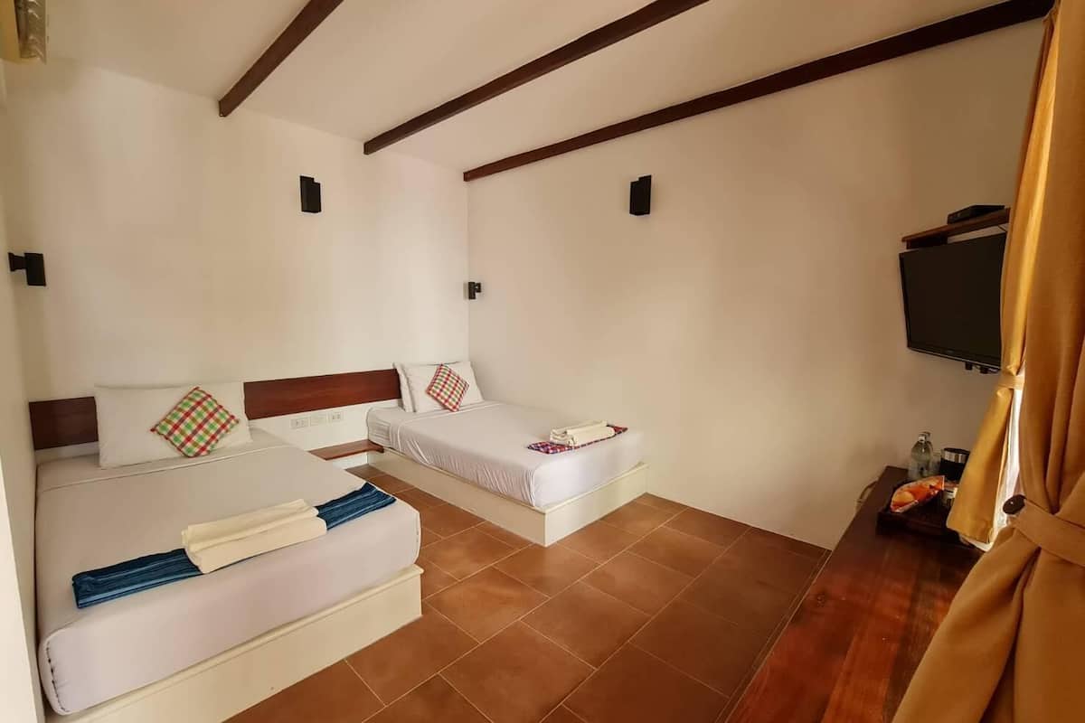 Quarto de hotel com duas camas, uma televisão e uma mesinha com uma garrafa e copos.