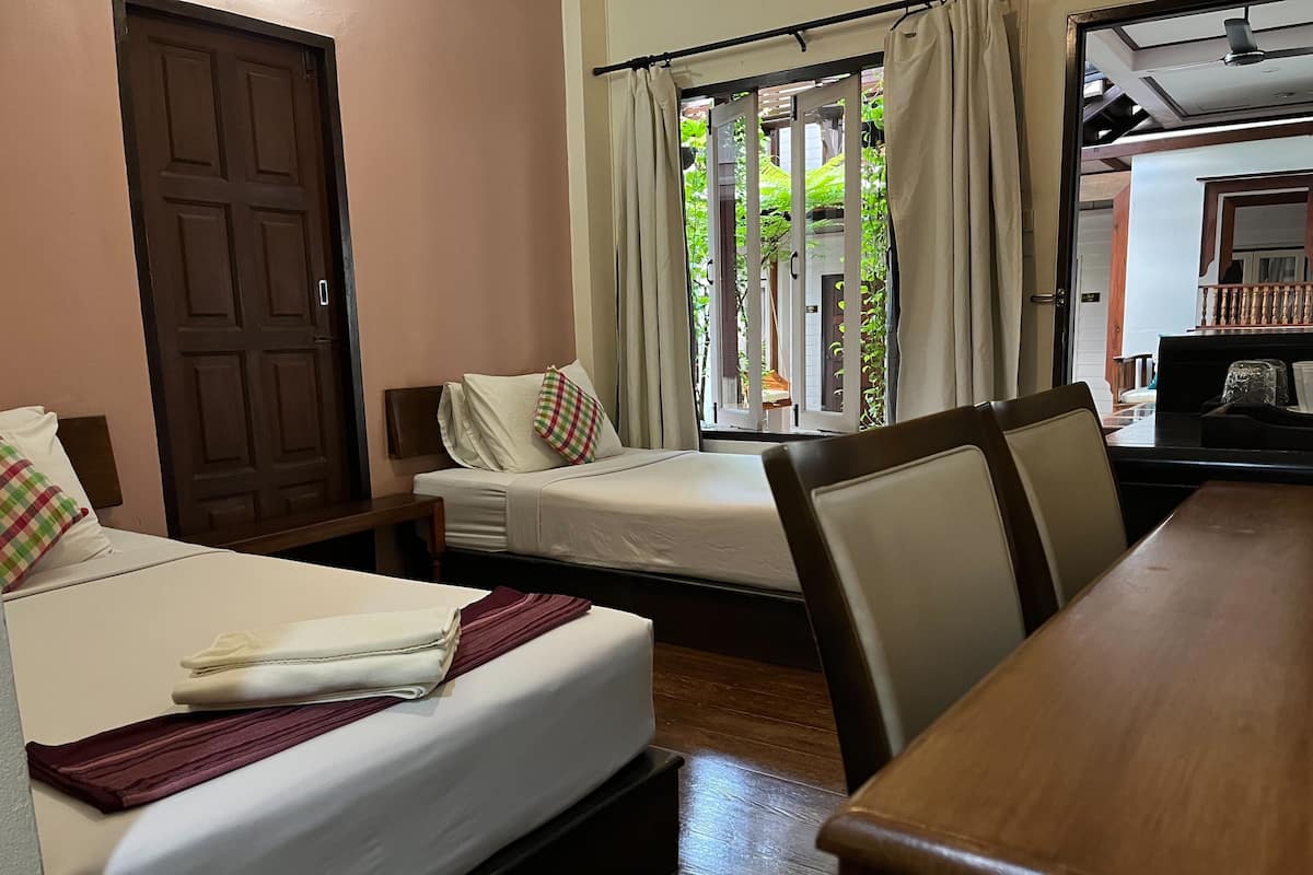 Quarto de hotel com duas camas, uma mesa de madeira e vista para o verde pela janela.