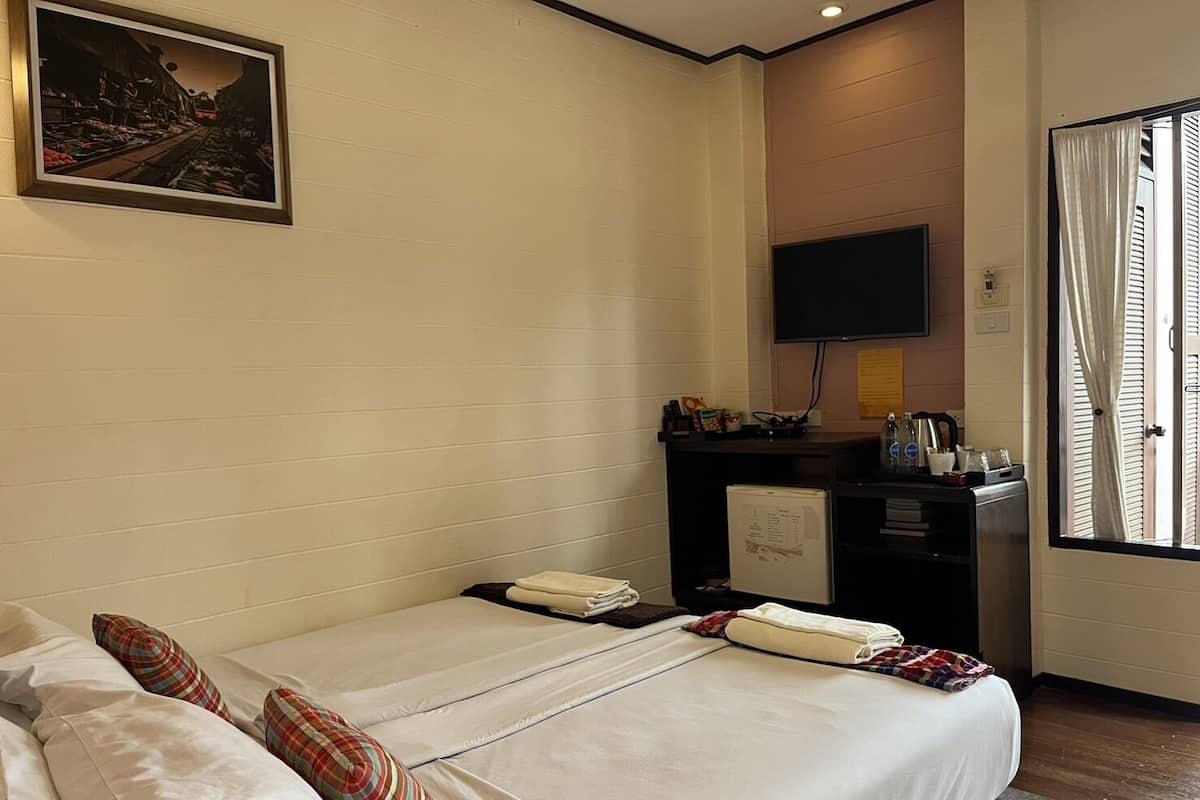 Quarto de hotel com cama, escrivaninha, televisão de tela plana, frigorífico e janela com cortinas.
