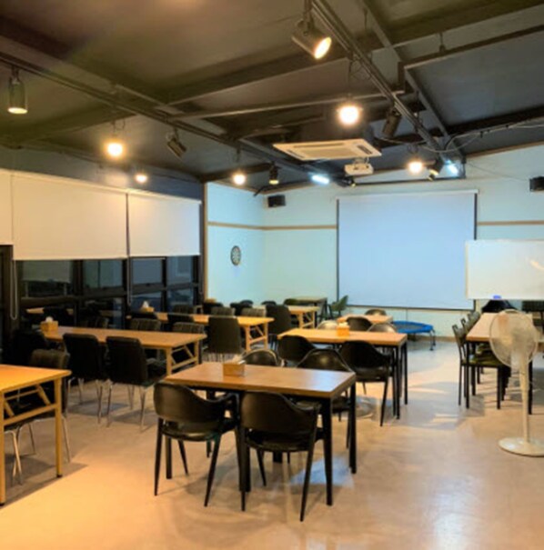 Uma sala de aula com mesas, cadeiras, uma tela de projetor e um relógio na parede.