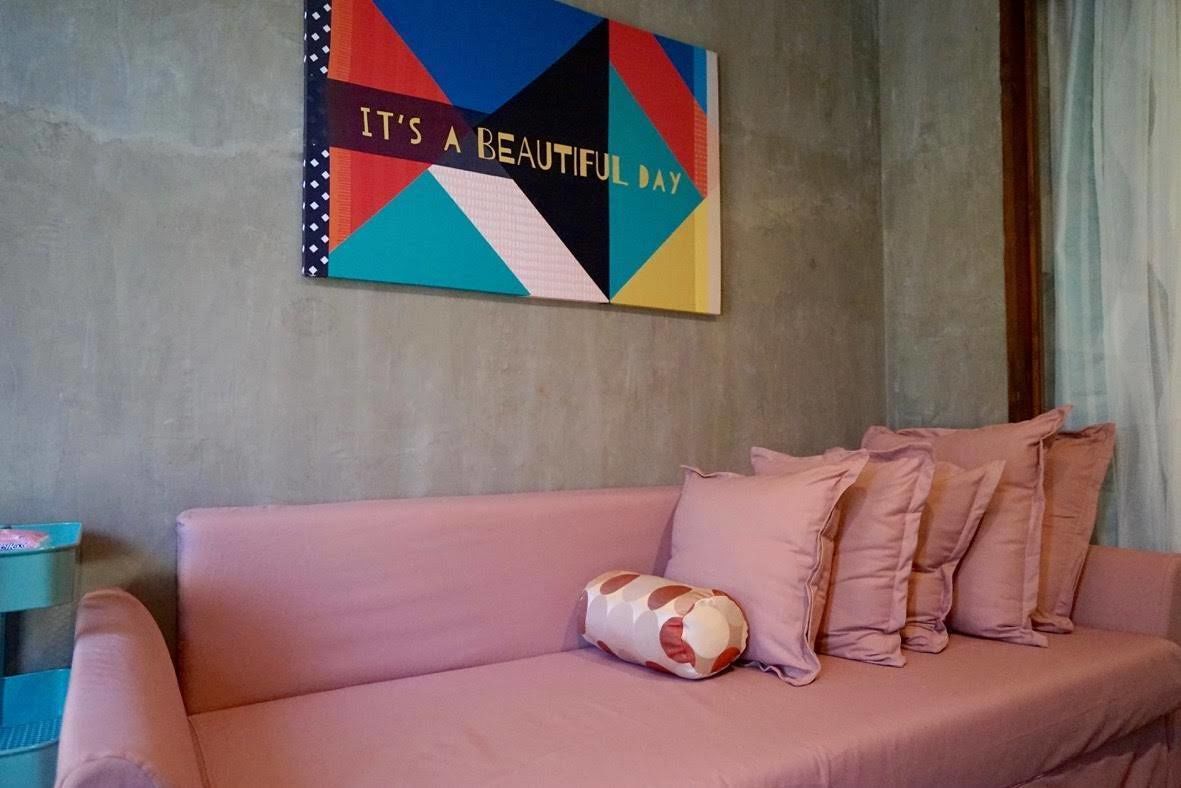 Um quarto com um sofá rosa, uma obra de arte geométrica colorida e uma almofada estampada.