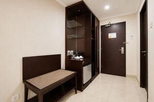 Quarto de hotel com uma cama, uma pequena escrivaninha com cadeira, um minibar e uma porta com um aviso.