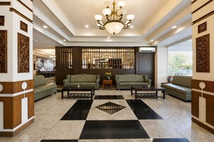 Um hall com dois sofás verdes, um candelabro e piso xadrez.
