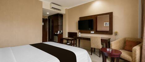 Quarto de hotel com cama, escrivaninha, cadeira, televisão e ar condicionado.