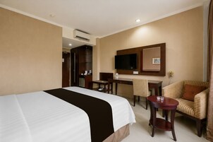 Quarto de hotel com cama, escrivaninha, cadeira, televisão e ar condicionado.