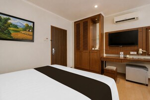 Quarto de hotel com cama, escrivaninha com televisão de tela plana, guarda-roupa e ar condicionado.