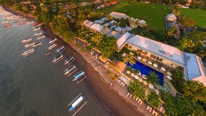 Vista aérea de uma área costeira com praia, barcos e um resort com piscina e área externa para sentar.