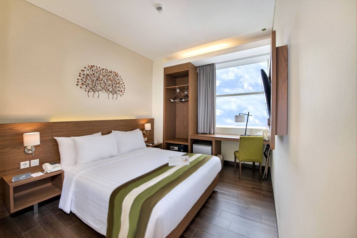 Quarto de hotel com uma cama grande, uma escrivaninha, uma cadeira, televisão e janela com vista para o céu.