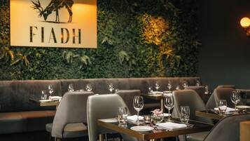 Interior de restaurante com parede verde, um letreiro com a inscrição "FIADH" e mesas montadas com copos e pratos.
