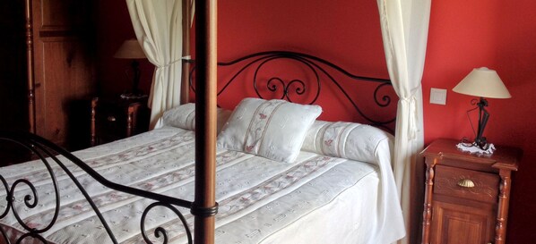Uma cama com dossel, uma mesa de cabeceira de madeira com abajur e uma parede vermelha.