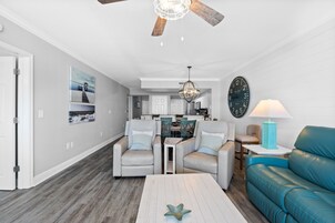 Uma sala de estar moderna com um sofá verde-água, poltronas brancas, uma mesa de centro e uma área de refeições ao fundo.