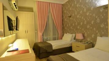 Quarto de hotel com duas camas, uma mesa, um guarda-roupa e uma janela com cortinas.