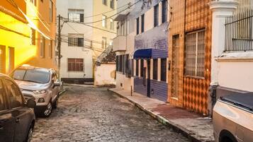 Uma rua de paralelepípedos ladeada por edifícios coloridos, carros estacionados e uma placa visível do Hostel da Providência.