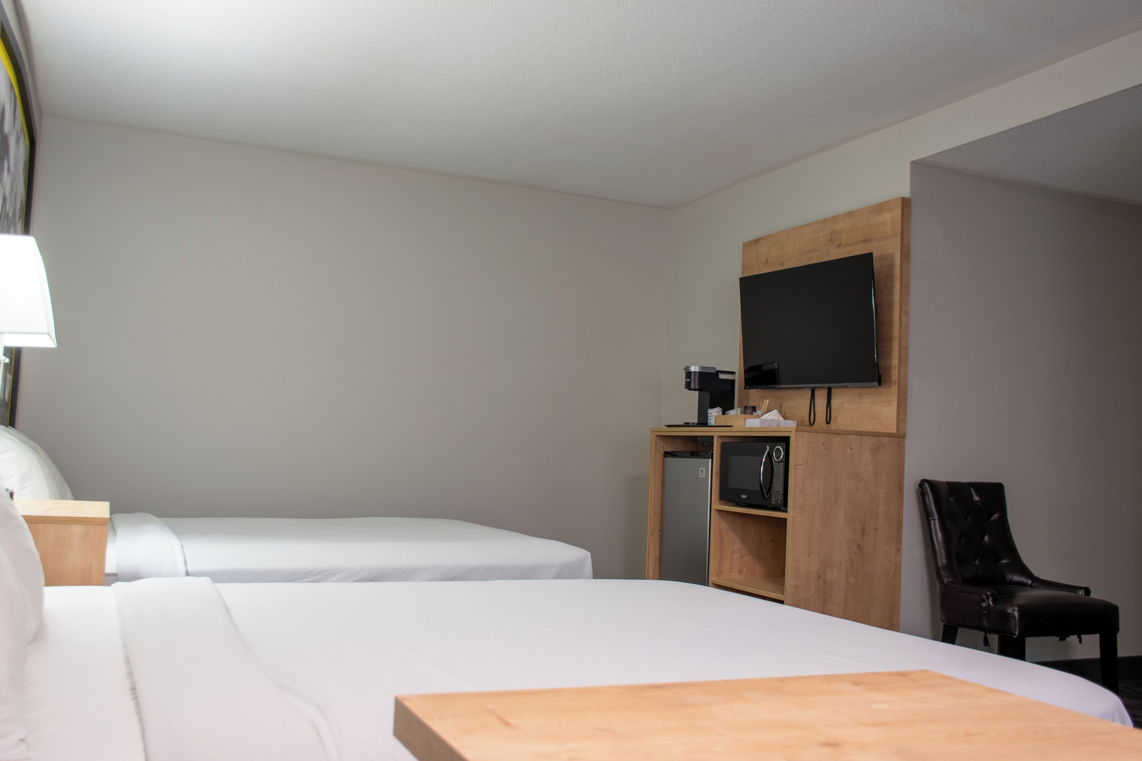 Quarto de hotel com duas camas de solteiro, uma escrivaninha de madeira, uma televisão sobre um suporte de madeira, uma cadeira e um pequeno frigorífico.