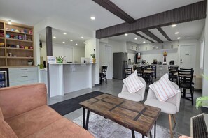 Uma sala de estar moderna com sofá, mesa de centro e área de cozinha com armários e geladeira.