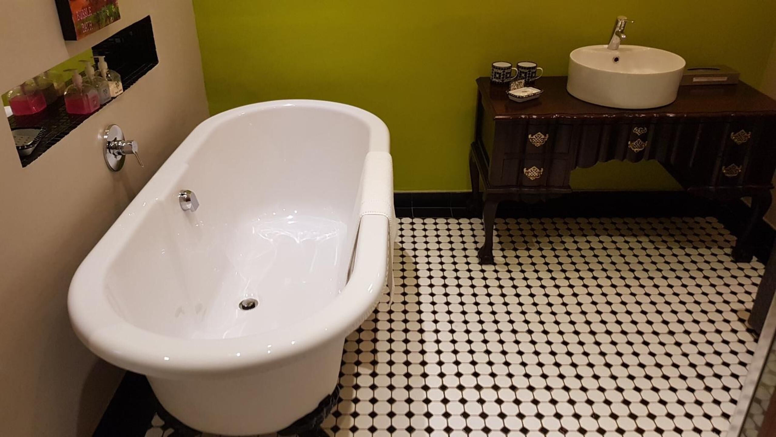 Casa de banho com banheira branca, lavatório e chão em mosaico.