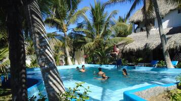 Piscina rodeada por palmeiras e um edifício com telhado de palha.
