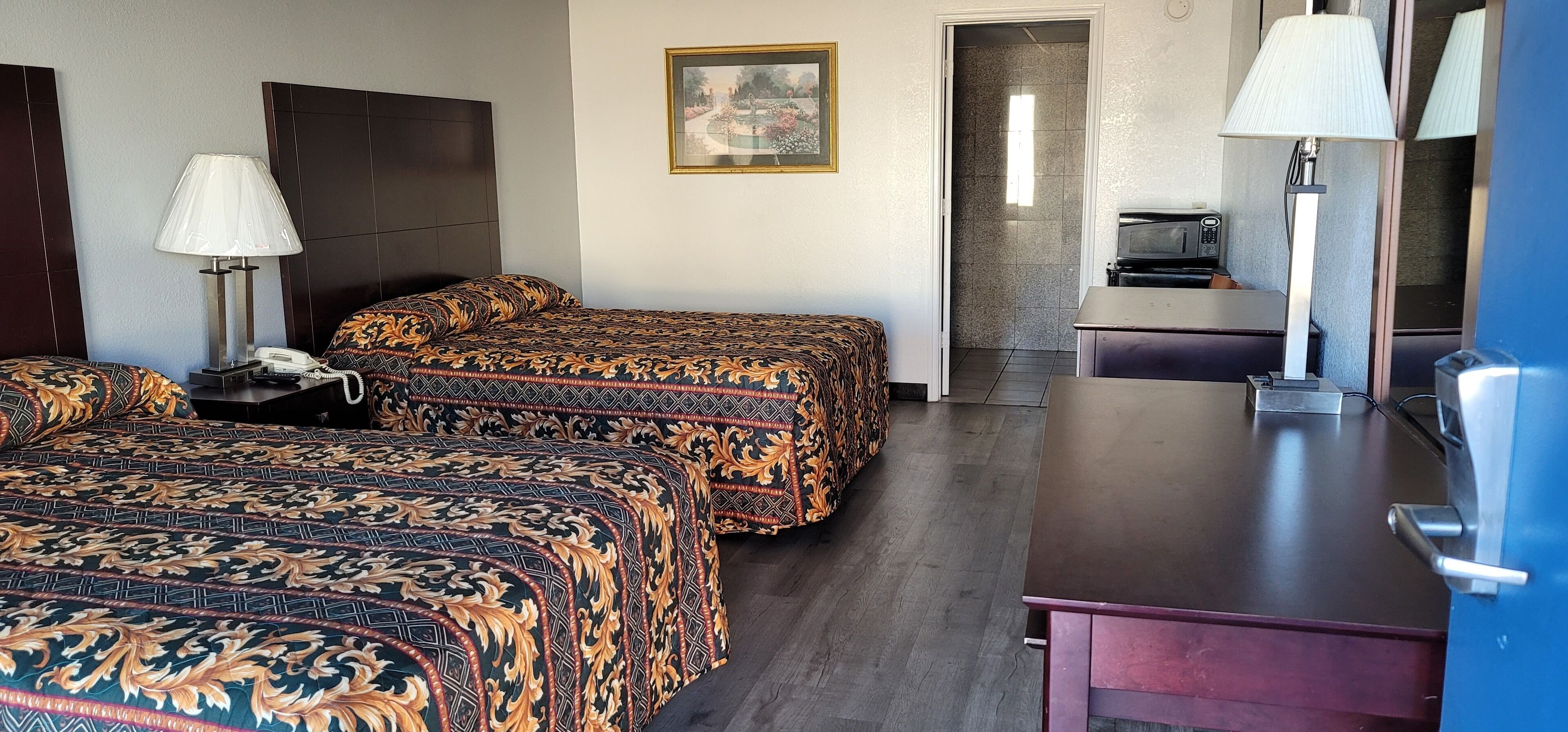 Quarto de hotel com duas camas, uma escrivaninha, telefone, abajur e um quadro na parede.