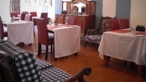 Uma área de refeições com mesas preparadas para quatro pessoas, cadeiras de madeira e um banco xadrez.