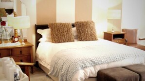 Quarto bem arrumado com uma cama grande, duas almofadas, mesa de cabeceira com abajur, criado-mudo e uma cadeira de madeira pequena.
