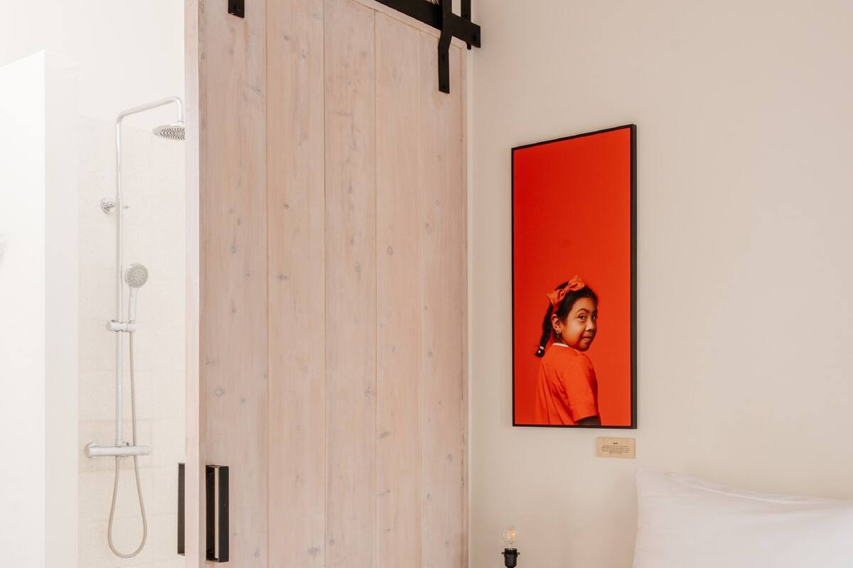 Quarto com cama, guarda-roupa de madeira, chuveiro e um quadro na parede.