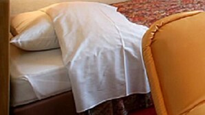 Cama com roupa de cama branca e um cobertor estampado.