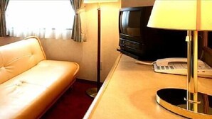 Quarto de hotel com sofá, televisão, abajur e telefone.
