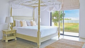 Uma cama de dossel com dossel, uma mesa de cabeceira com abajur, e vista para um lago através de janelas amplas.