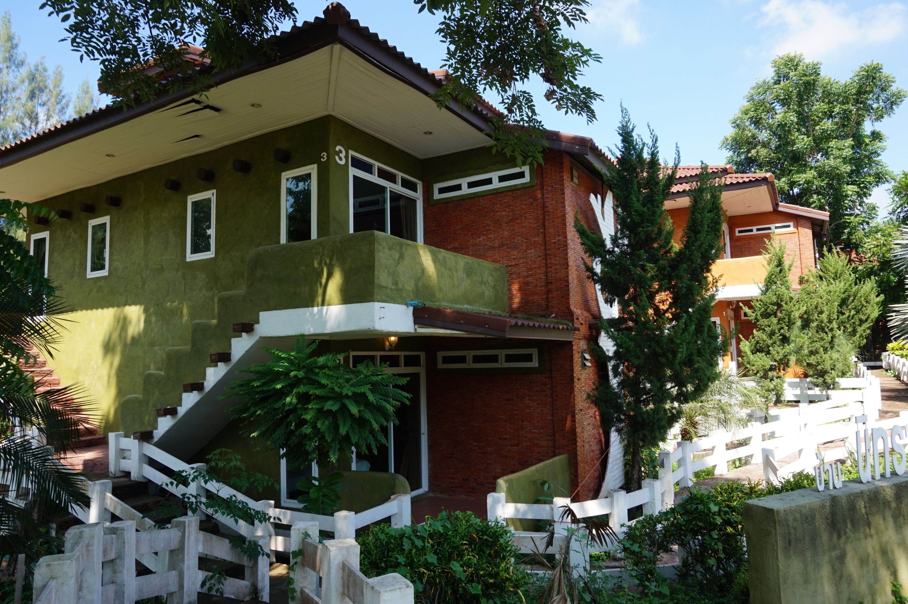 Uma casa de dois andares com fachada de tijolos, uma varanda e um cercado branco.